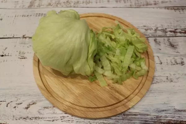 Kochan Iceberg og skiver salat på en rund skærebræt lavet af træ