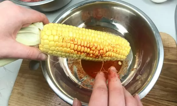 Corriendo la mazorca de maíz con una mezcla de aceite crema derretido y pimiento rojo molido