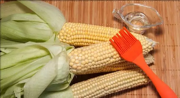 Kolby kukurydzy z wygiętymi liśćmi, olej roślinnym i kulinarną szczotką na stole