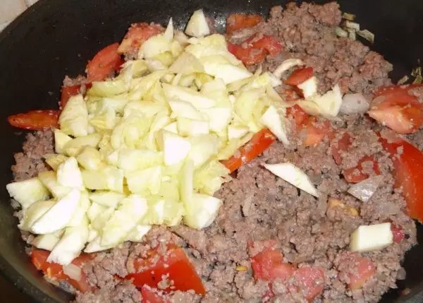 Carne picada, rollos arrugados de calabacín y cubos en rodajas de tomates en una sartén.