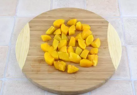 Hiniwa ng maliliit na piraso ng de-latang peaches sa isang round cutting board