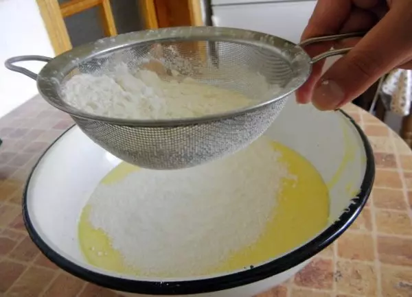 Sift tepung dalam mangkuk dengan campuran telur dengan saringan logam