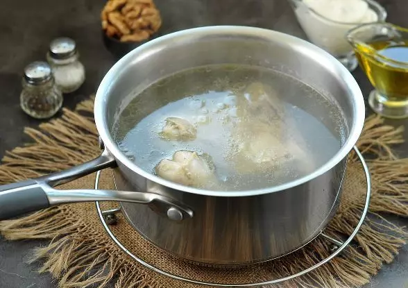ชิ้นส่วนของไก่และน้ำซุปในกระทะโลหะที่มีด้ามจับบนโต๊ะ