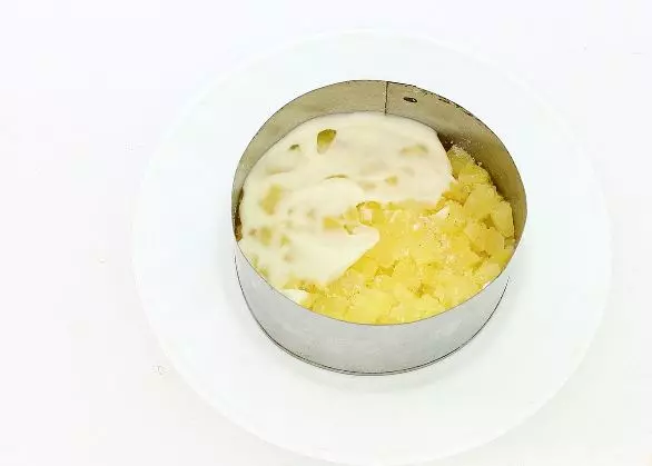 Una capa de papas hervidas con mayonesa en un anillo de moldeo de metal en un plato