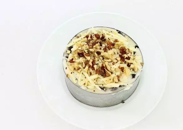 Decorated with grated solid cheese and chopped walnuts salad in molding ring on a plate