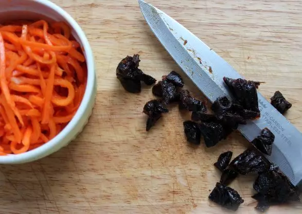 Prunei tăiate, cuțit și morcovi în coreeană într-un castron de pe masă