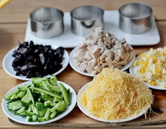 टेबल पर चिकन, प्रून, चावल और खीरे के साथ सलाद खाना पकाने के लिए उत्पाद