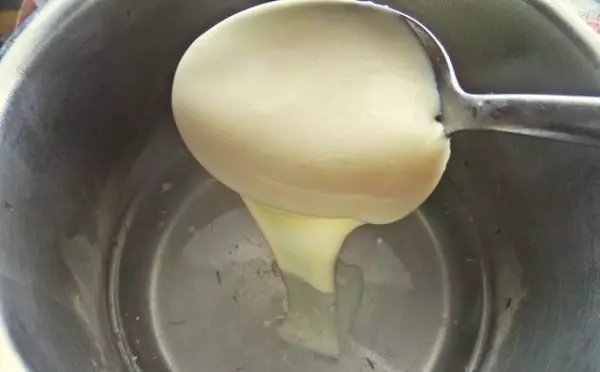 Spoon with melted cheese over saucepan with water