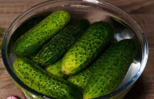 Freshanananan ƙananan cucumbers a cikin gilashin kwano da ruwa a kan tebur