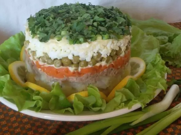Puff-Salat von der Cod-Leber- und Konserven-Grüner Erbsen auf einem Teller mit Kopfsalatblättern und Zitronenscheiben