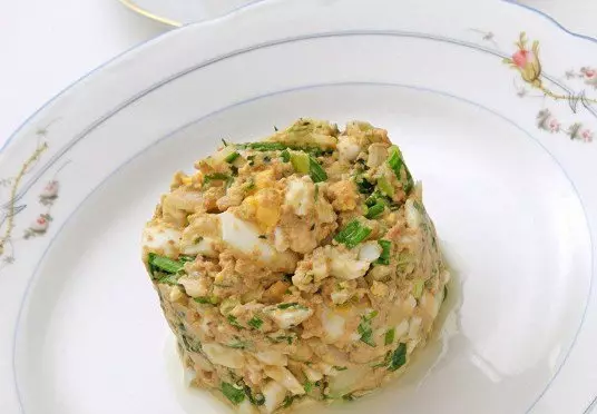 Porzione di insalata di fegato di merluzzo, uova e cipolle verdi su un grande piatto con motivi floreali