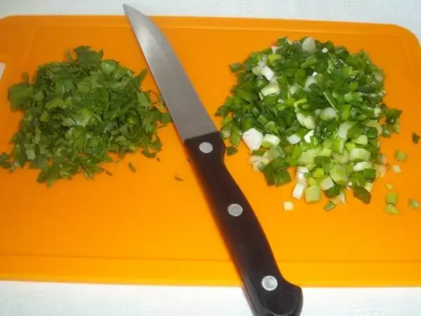 Sitno sjeckana svježa zelenila i nož s crnom ručkom na narančastoj ploči za rezanje