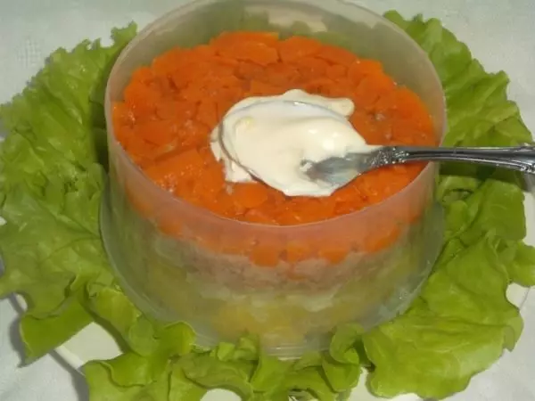 Camada de cenoura cozida no anel de moldagem e colher de metal com maionese