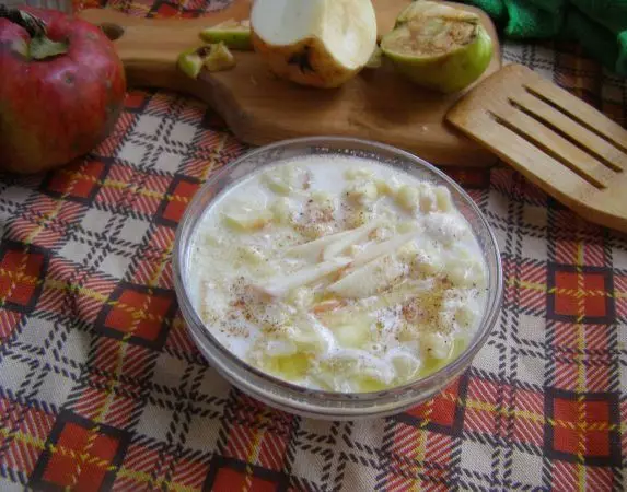 Sopa de leche con vermicellina y manzanas sobre la mesa con un mantel a cuadros.