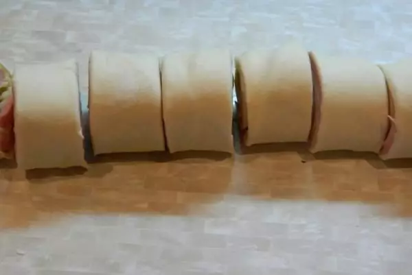 Нарізану порційними шматочками рулет з сирого тесту з ковбасою і сиром на столі