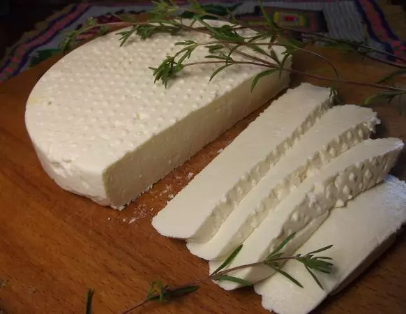 Bir ahşap kesme tahtası üzerinde yeşillik ile dilimler ile kesilmiş Adygei peyniri
