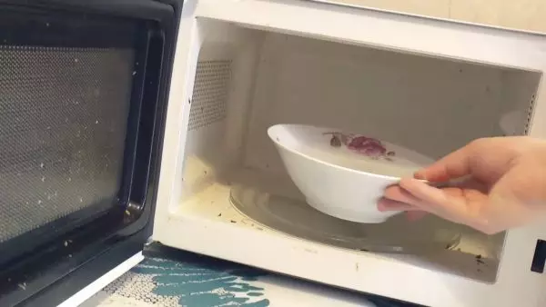 Nainen asettaa levyn keittoon likaisessa mikroaaltouunissa