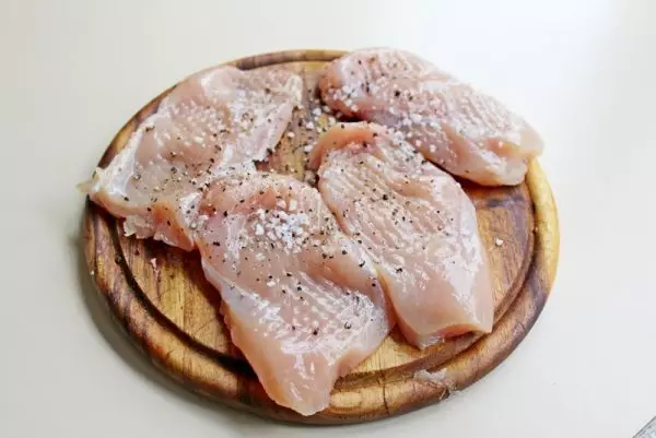 Salt and black ground pepper pieces of chicken fillet on a cutting board