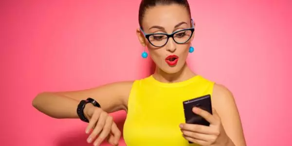 Mädchen in einem gelben T-Shirt und stilvolle Gläser schaut auf das Telefon, die ihre Hand mit einer Uhr anheben