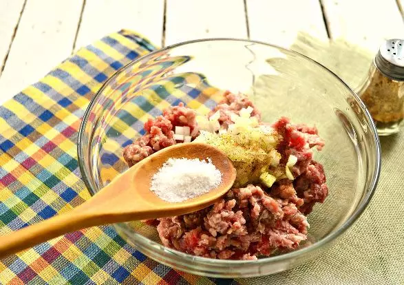Carne picada de carne con una abundancia en un recipiente de vidrio y sal en una cuchara de madera.