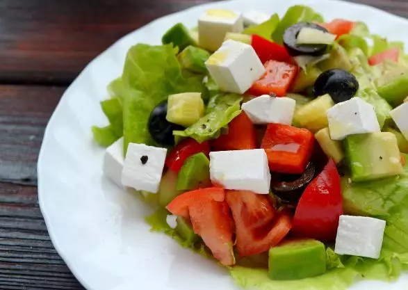 एक बड़ी सफेद प्लेट पर सब्जियों और पनीर के साथ एवोकैडो के तैयार सलाद