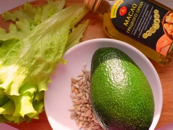 Salatne liste, avokado in sončnična semena v ploščici, steklenico z maslom masla na mizi