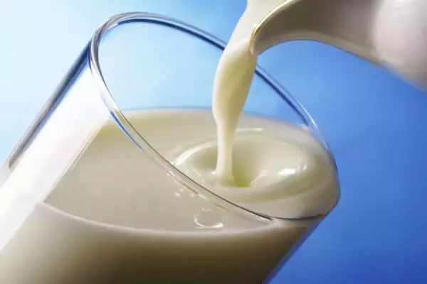 Milch aus einem Krug in ein Glas gegossen
